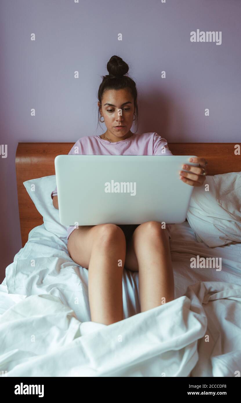 Young woman teleworking while making videocall on laptop and sitting on ...