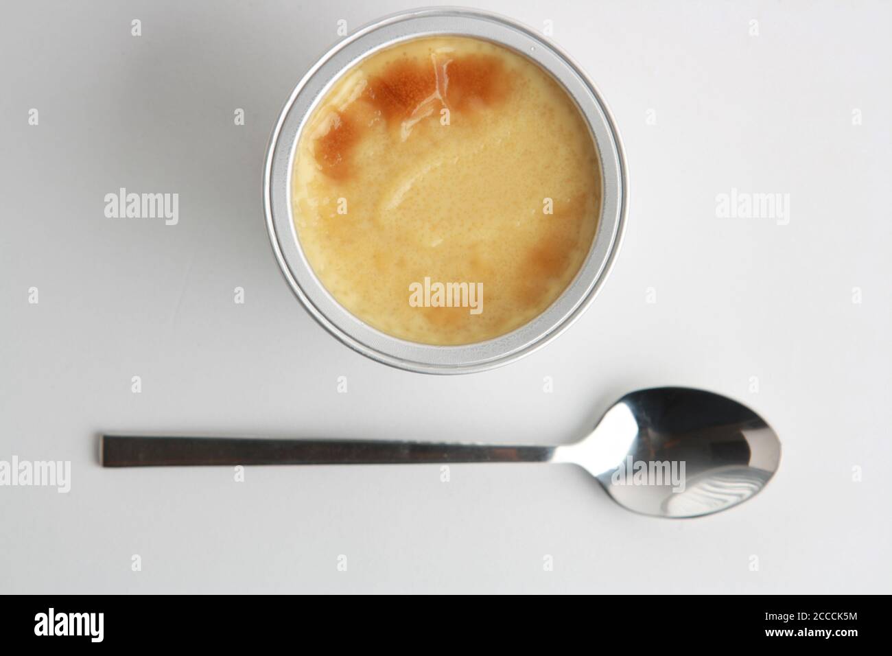 Delicious egg flan in an aluminum container and a spoon on a white ...