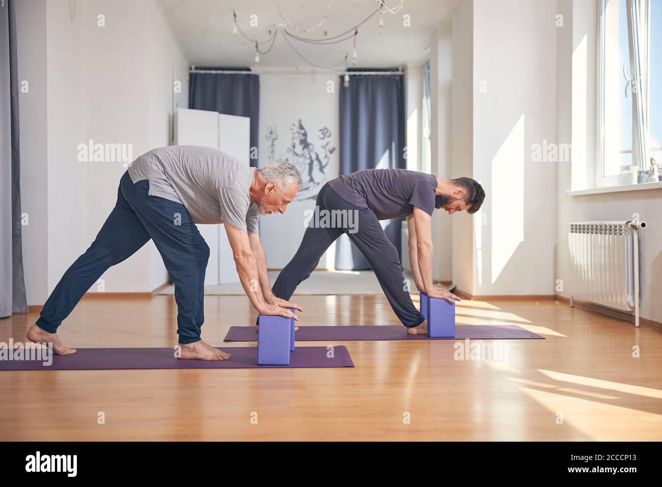 Two men performing a standing forward bend Stock Photo - Alamy