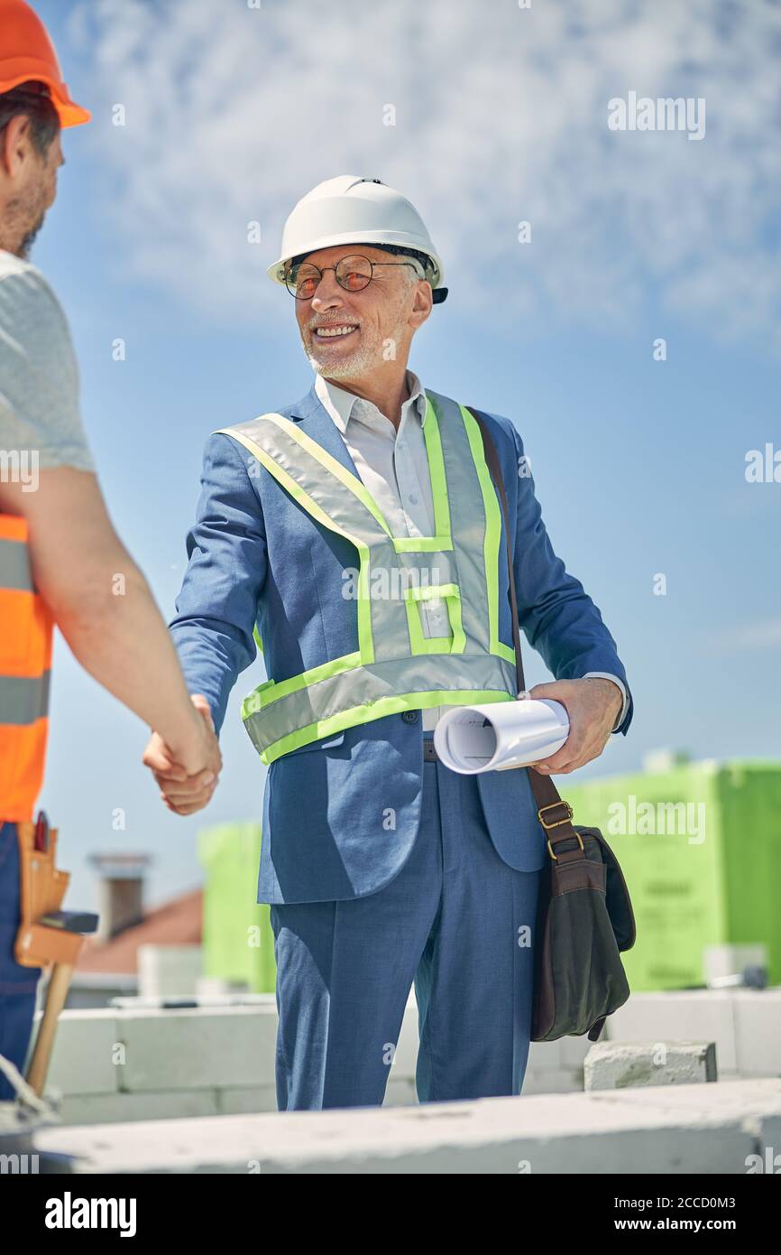 Smiling foreman with house plans looking at a builder Stock Photo - Alamy