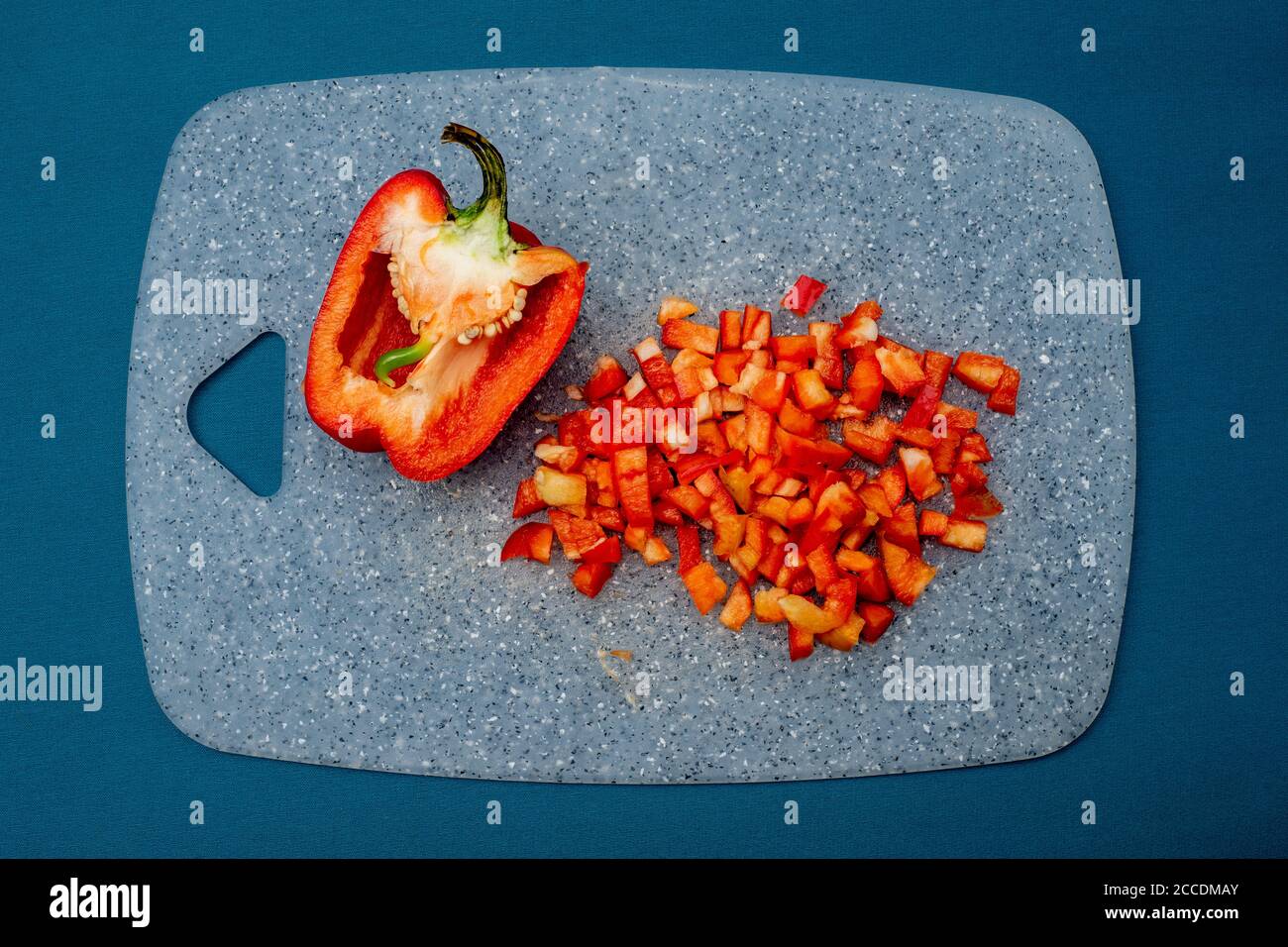 Top view of a cut in half and chopped red pepper on a blue board and ...