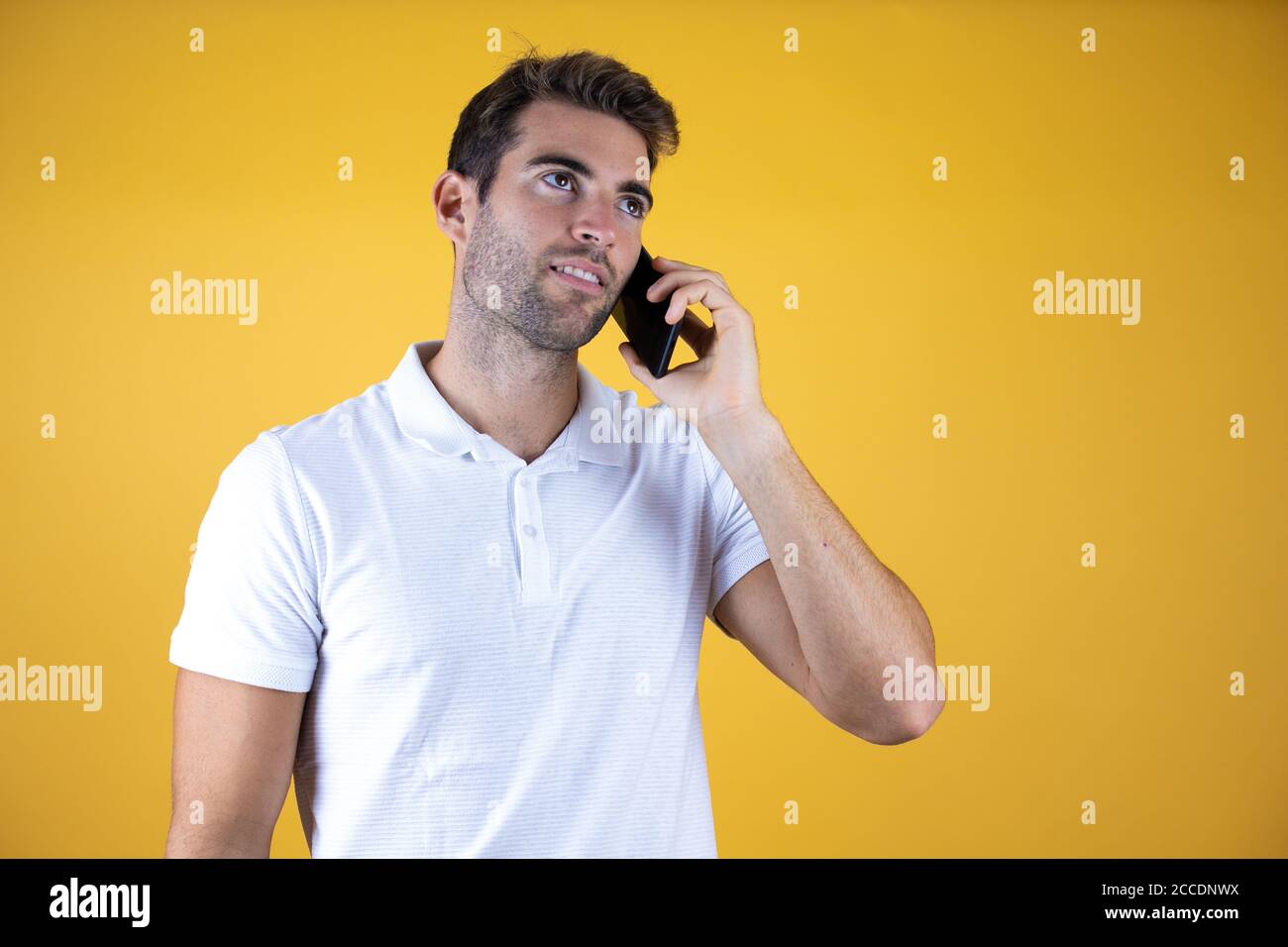Young man having a conversation using smartphone over yellow background ...
