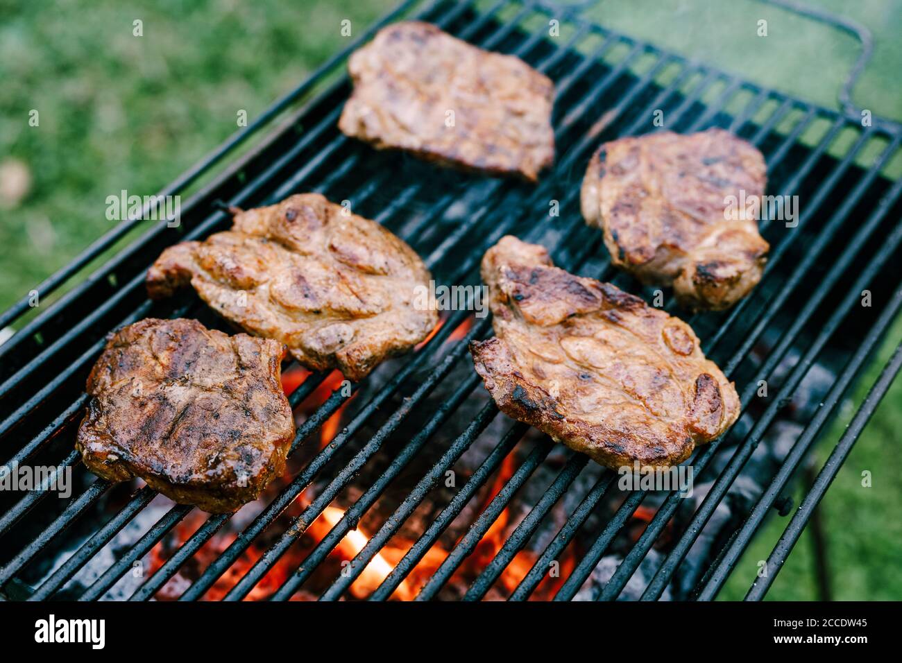 Five steaks on a metal grill are fried on coals in the grill Stock ...