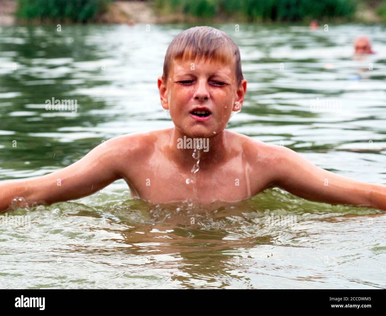 Water runs down the face of a Caucasian boy emerging from the lake ...