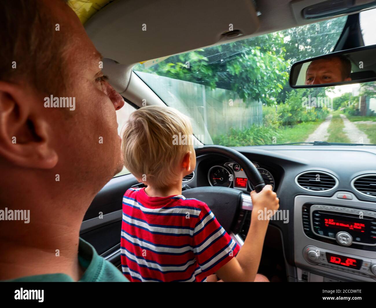 Little caucasian boy drives a car sitting on his daddy's lap Stock ...