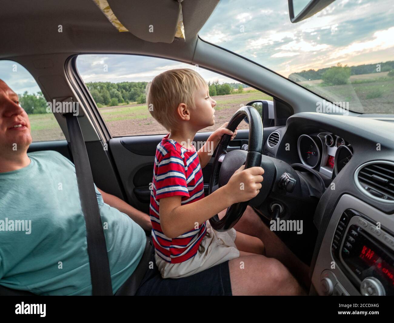 Little caucasian boy drives a car sitting on his daddy's lap Stock ...