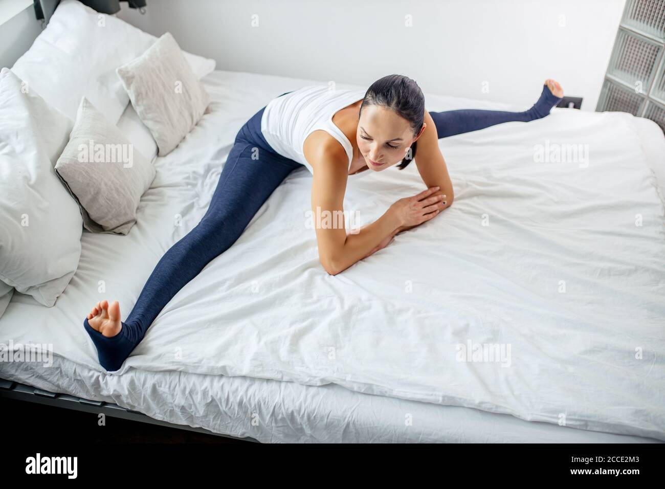 young caucasian sporty slender woman sit in a twine on bed at home ...