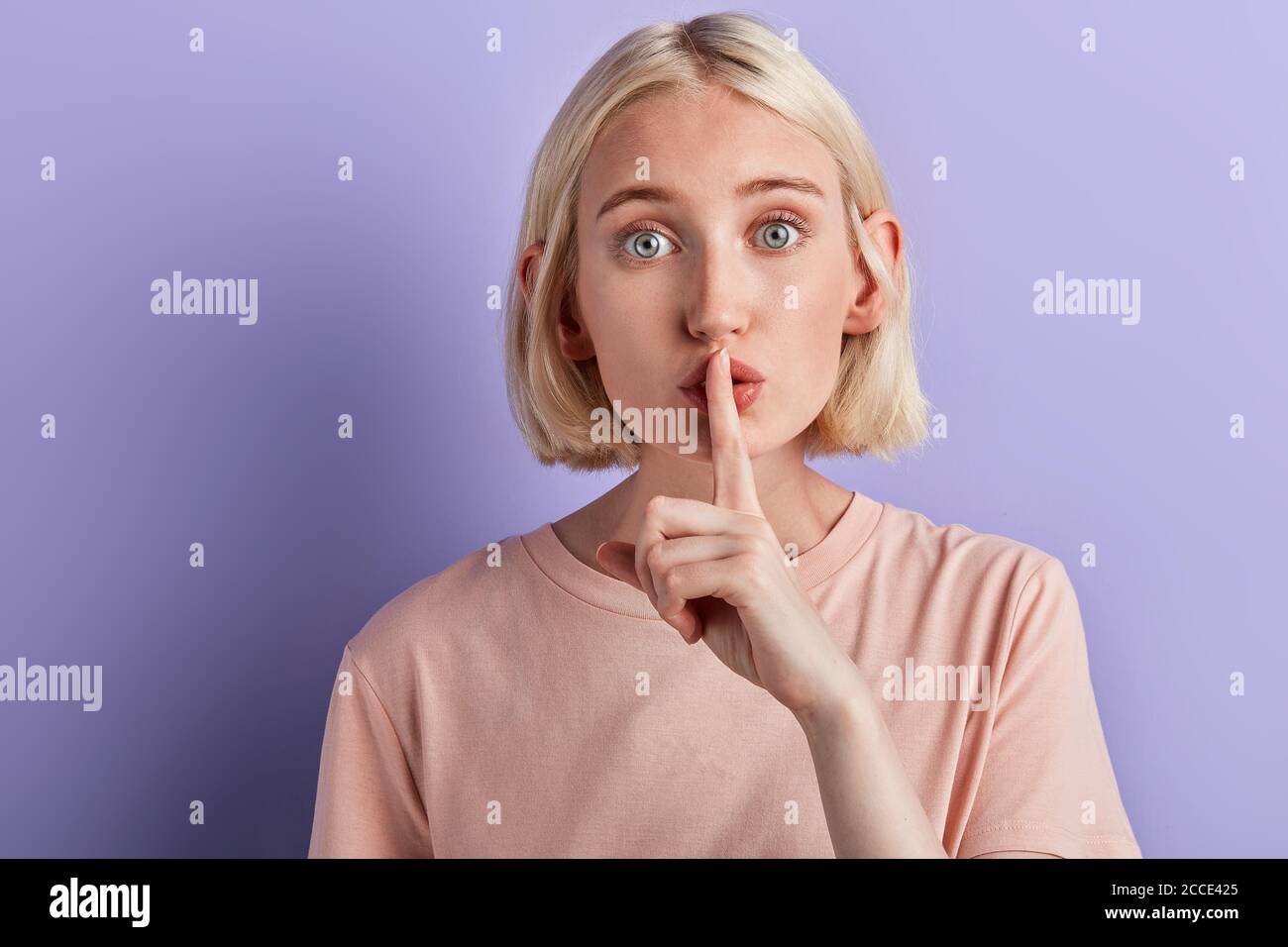 beautiful blonde girl showing shhh sign with finger to lips over violet ...