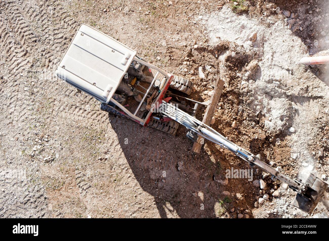 Mini excavator, seen from above, working on dusty ground breaks stone ...