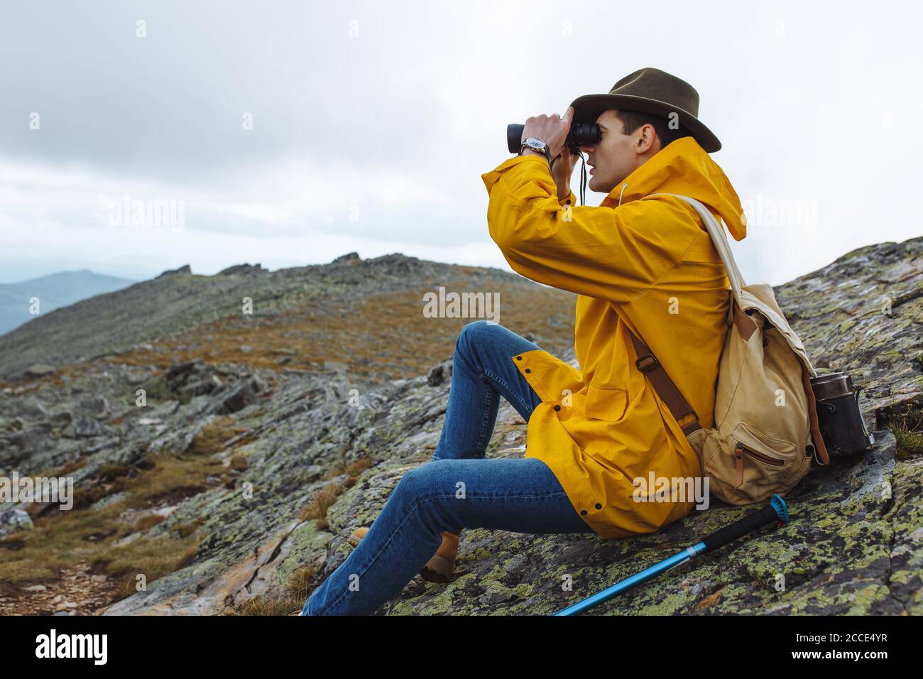 stylish hikers in raincoat, green hat with backpack holding binoculars ...