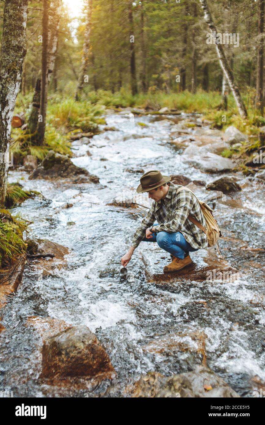 active tourist taking water into his cup from the river, full length ...
