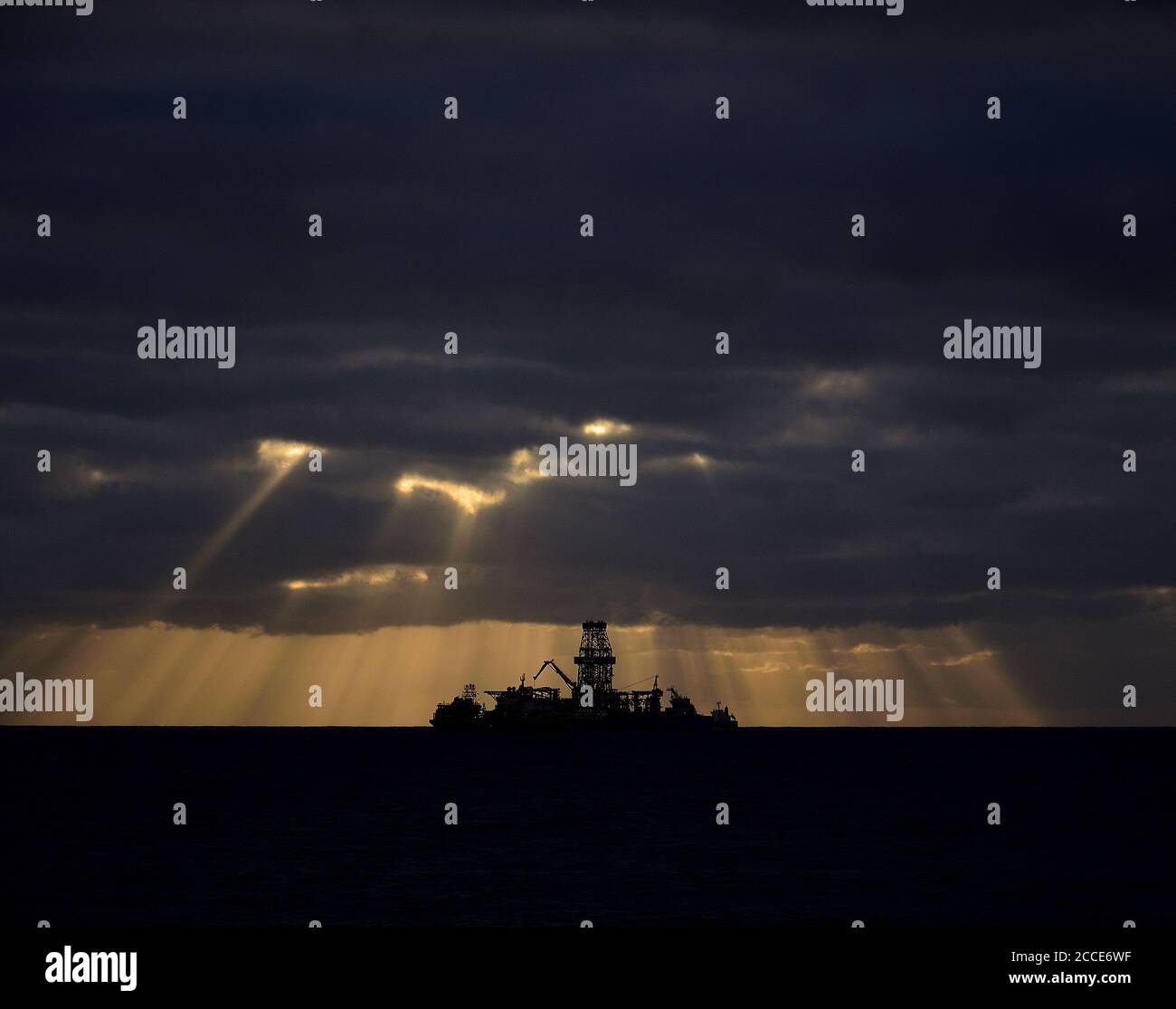 Backlit oil rig at dawn, cloudy sky and beams of light through the ...