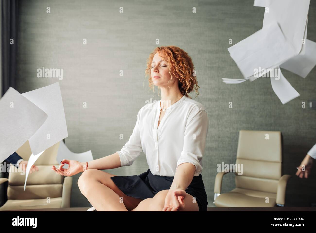 Calm young red-haired woman in formal wear having yoga meditation on ...