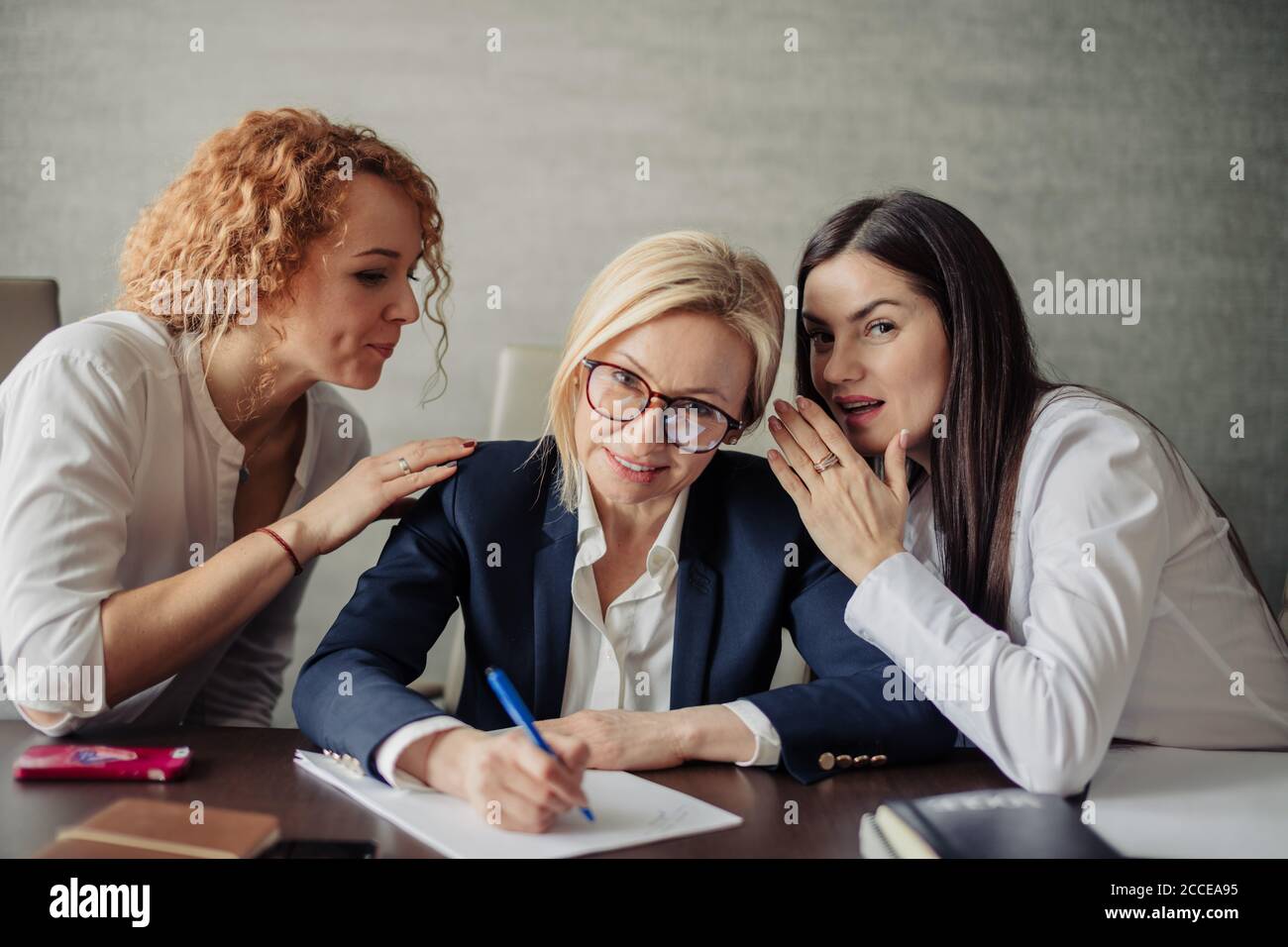 Young female gossipers employees working together discussing rumors ...