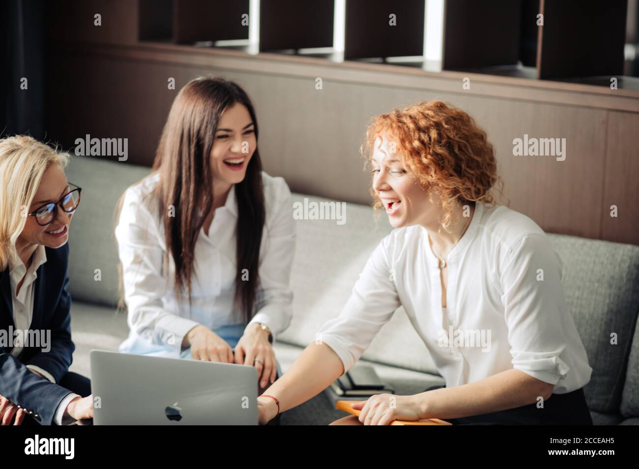 Red haired female corporate mentor helping two young women employees ...
