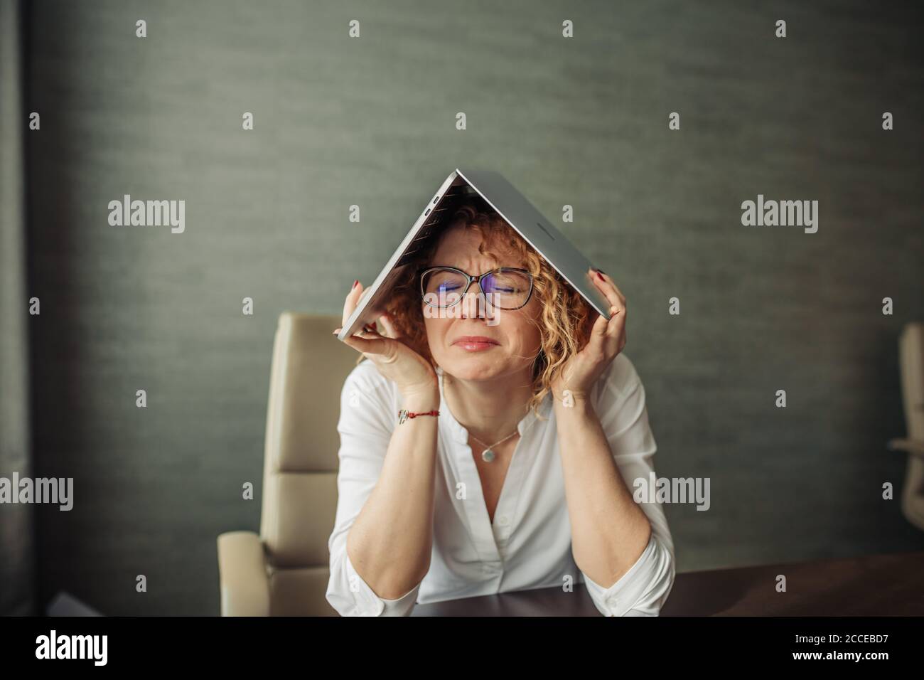 Young tired overworked woman keeps laptop computer over head, closes ...