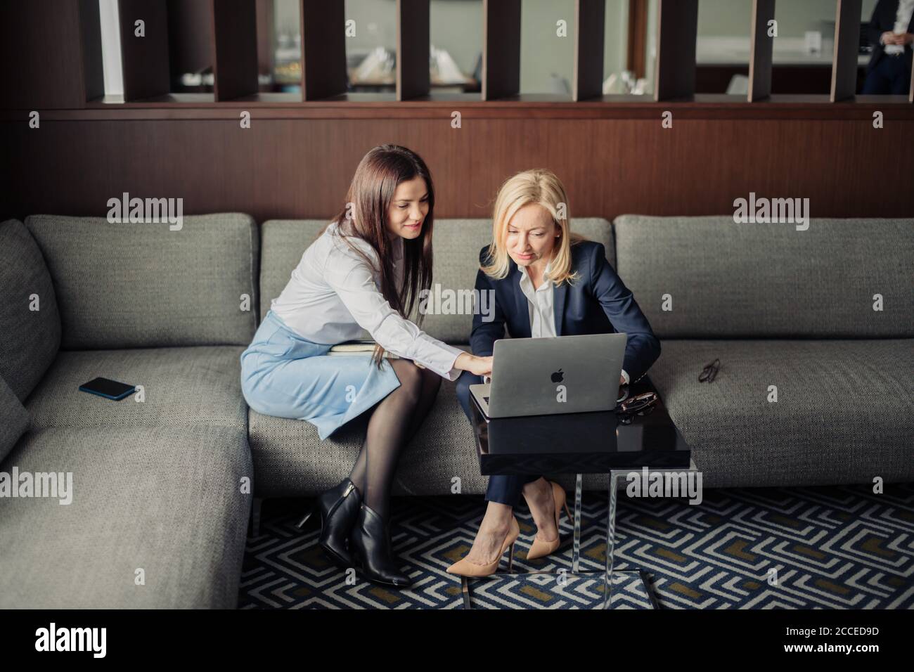 Two smiling female employees co-working on line with a laptop sitting ...