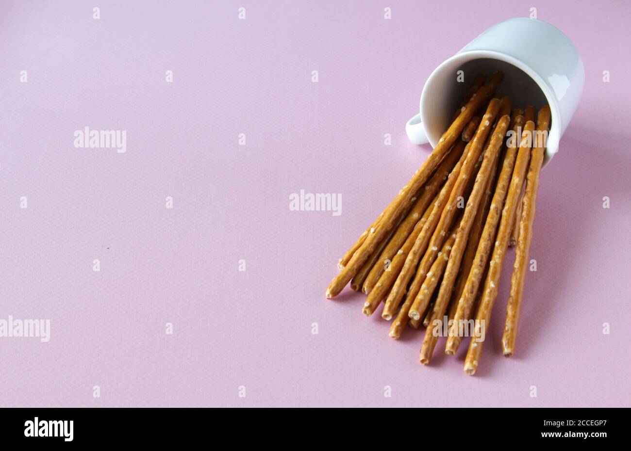 Bread sticks knocked over white cup on the pink background with copy ...
