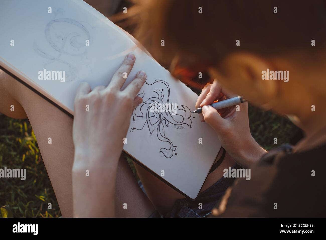 Woman draws letters in the park. Outline hand lettering in a sketchbook ...