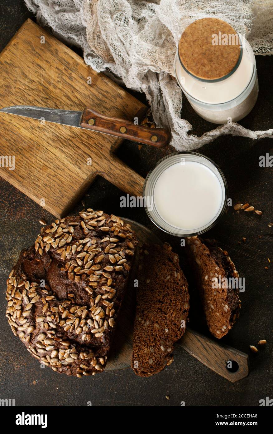 Homemade rustic rye bread with sunflower seeds and a bottle of milk on ...