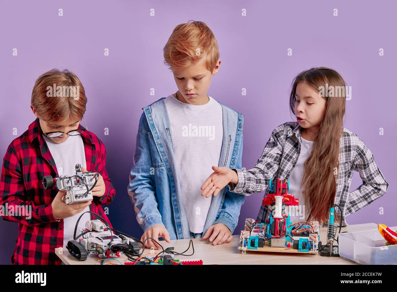 portrait of enthusiastic three kids working as team, assembling robots ...