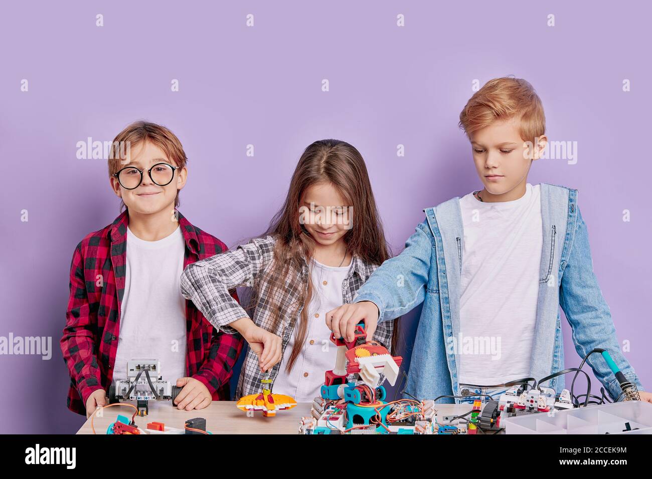 portrait of enthusiastic three kids working as team, assembling robots ...