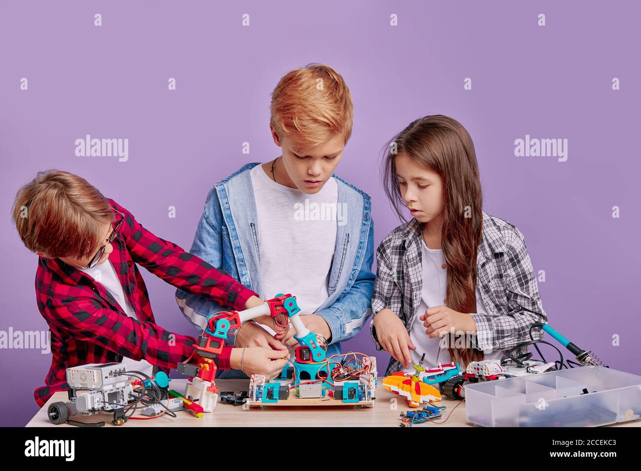 portrait of enthusiastic three kids working as team, assembling robots ...