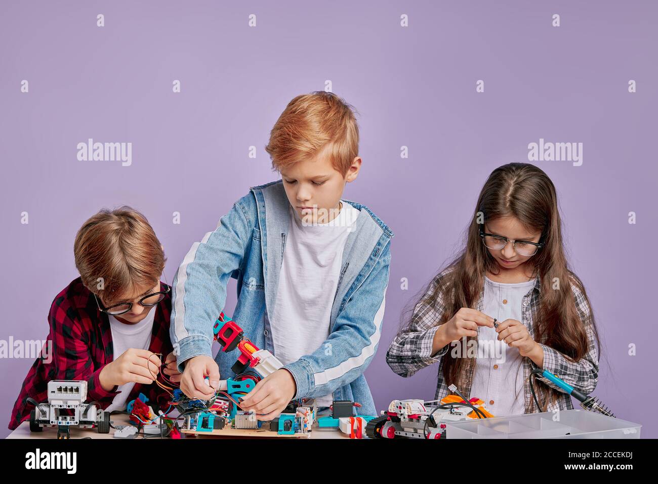 portrait of enthusiastic three kids working as team, assembling robots ...