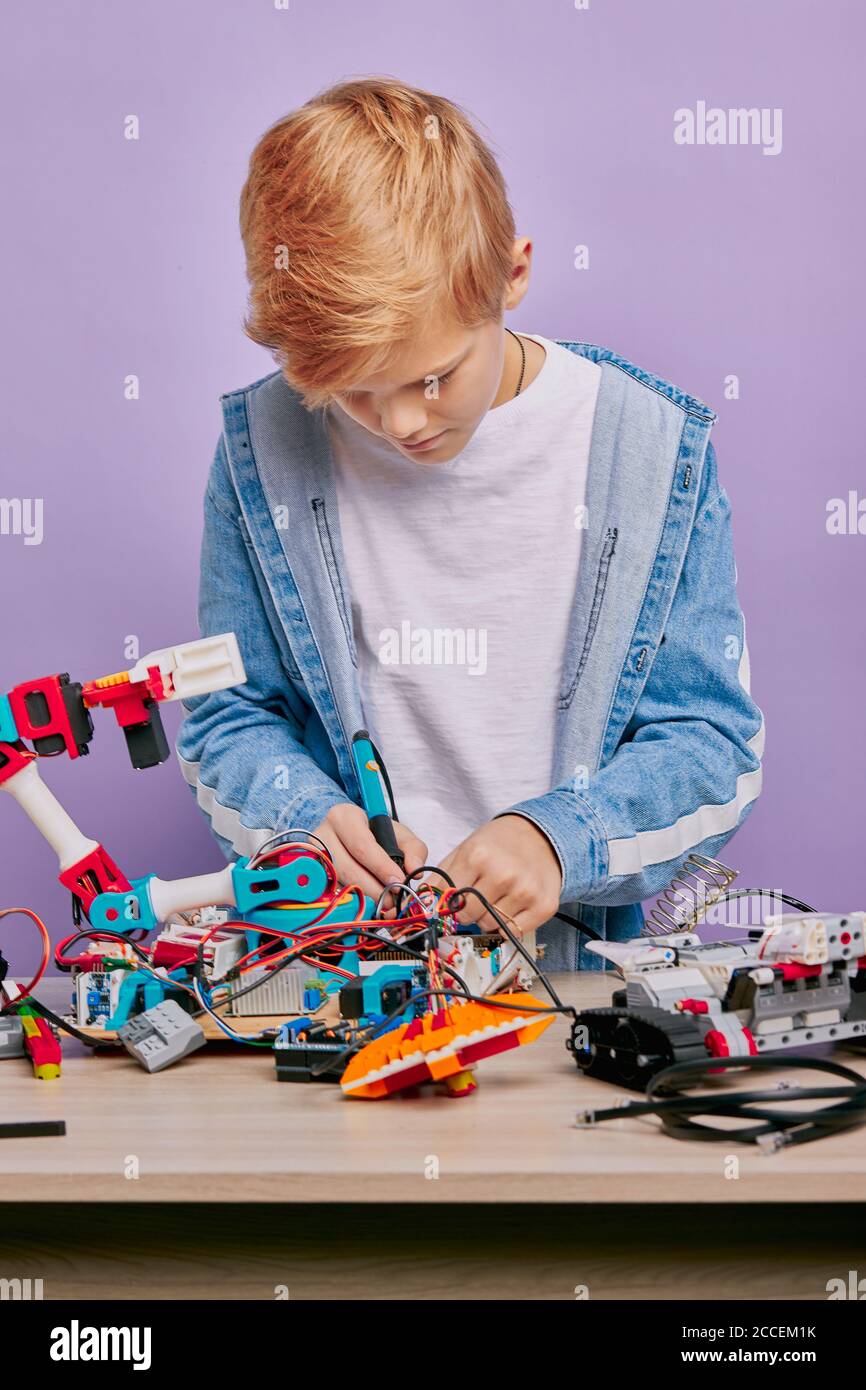 portrait of smart kid boy interestedly studying robots, assembling ...