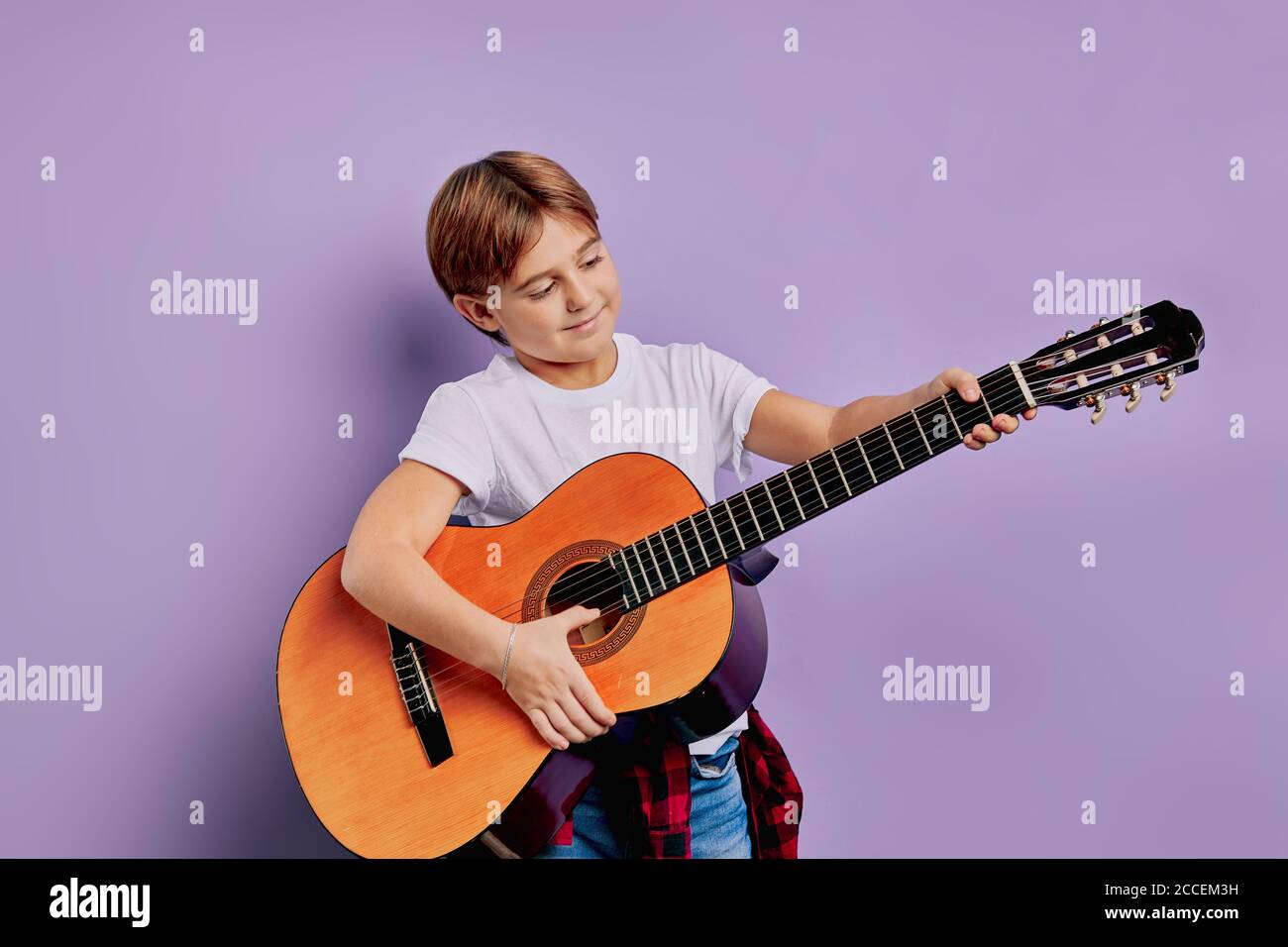 portrait of talented kid boy holding acoustic guitar and try to play on ...