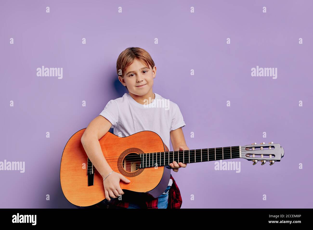 portrait of talented caucasian kid boy holding acoustic guitar and try ...