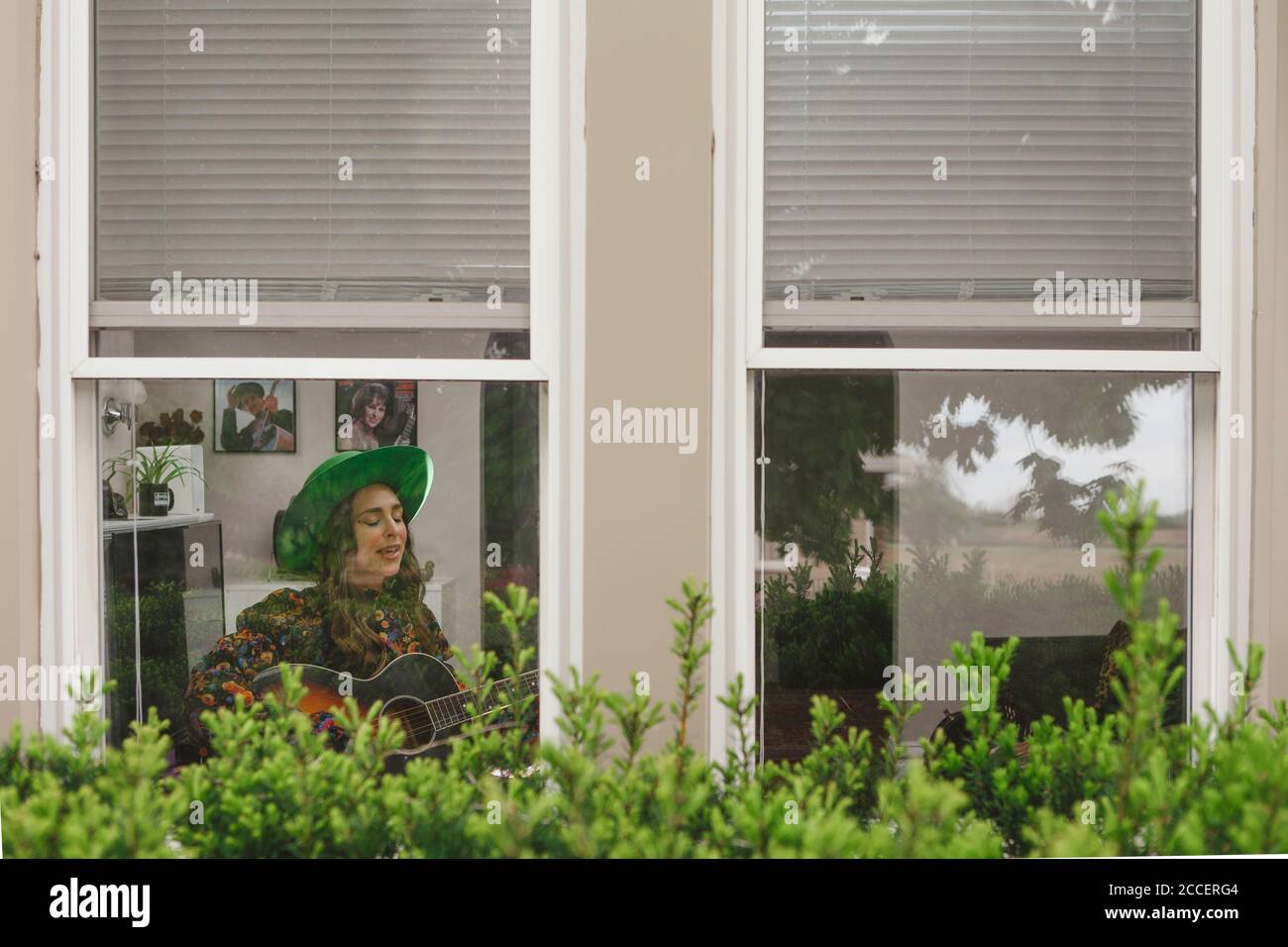 A woman sits singing at a window playing guitar in living room at home ...