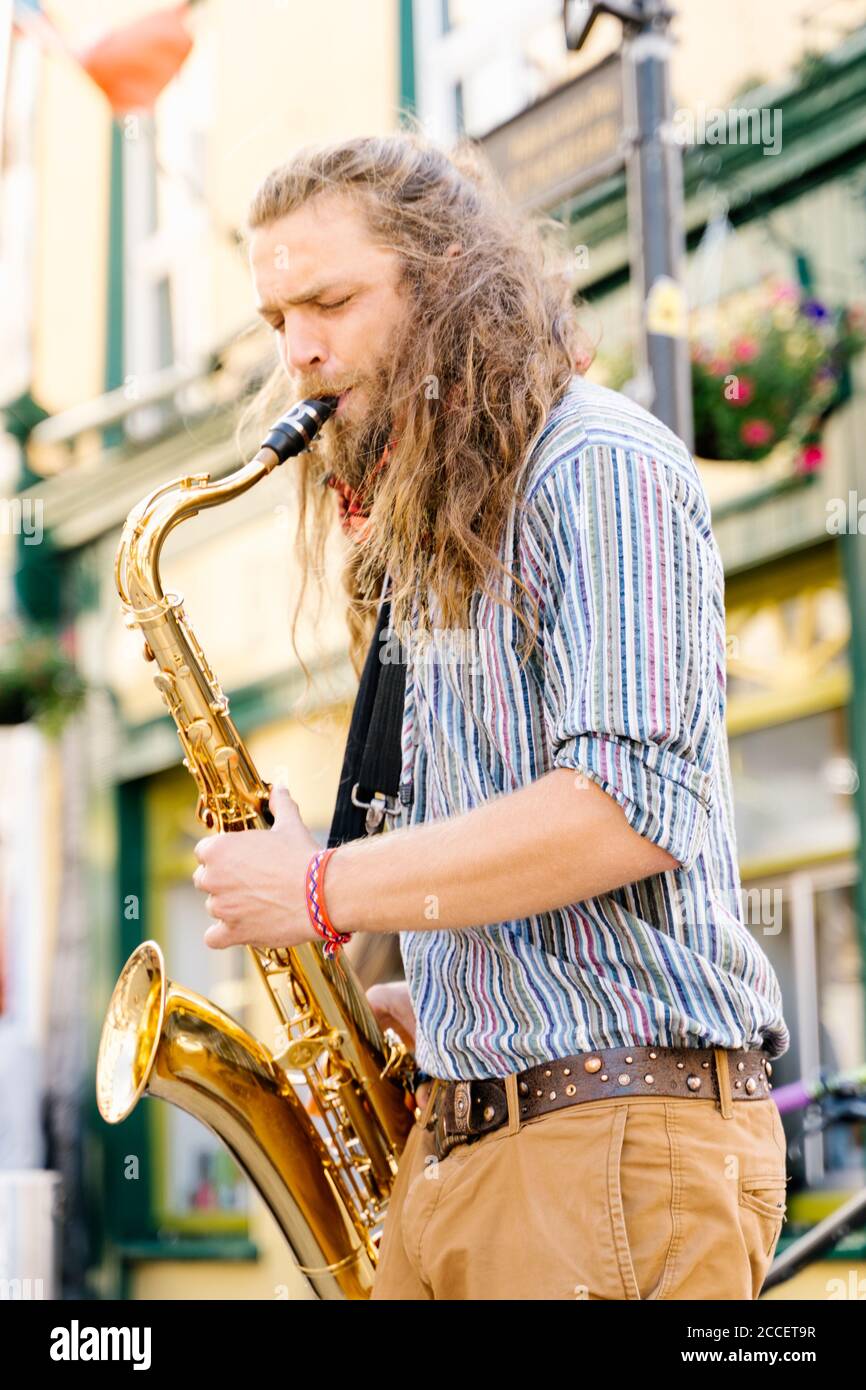 Vertical photo of a young man with long hair playing saxophone in the ...