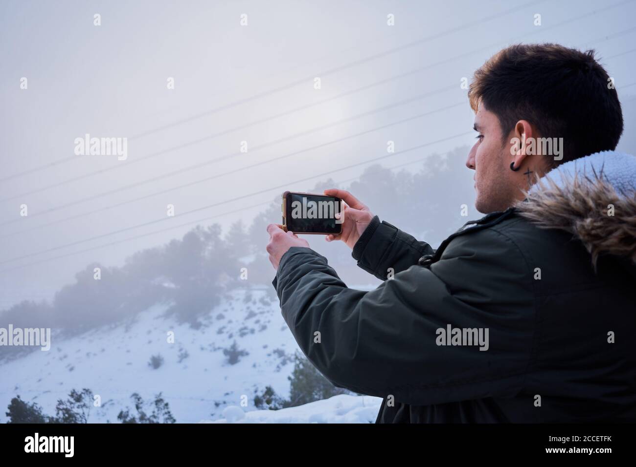 A young latin man takes a photo with his phone surrounded by snow Stock ...