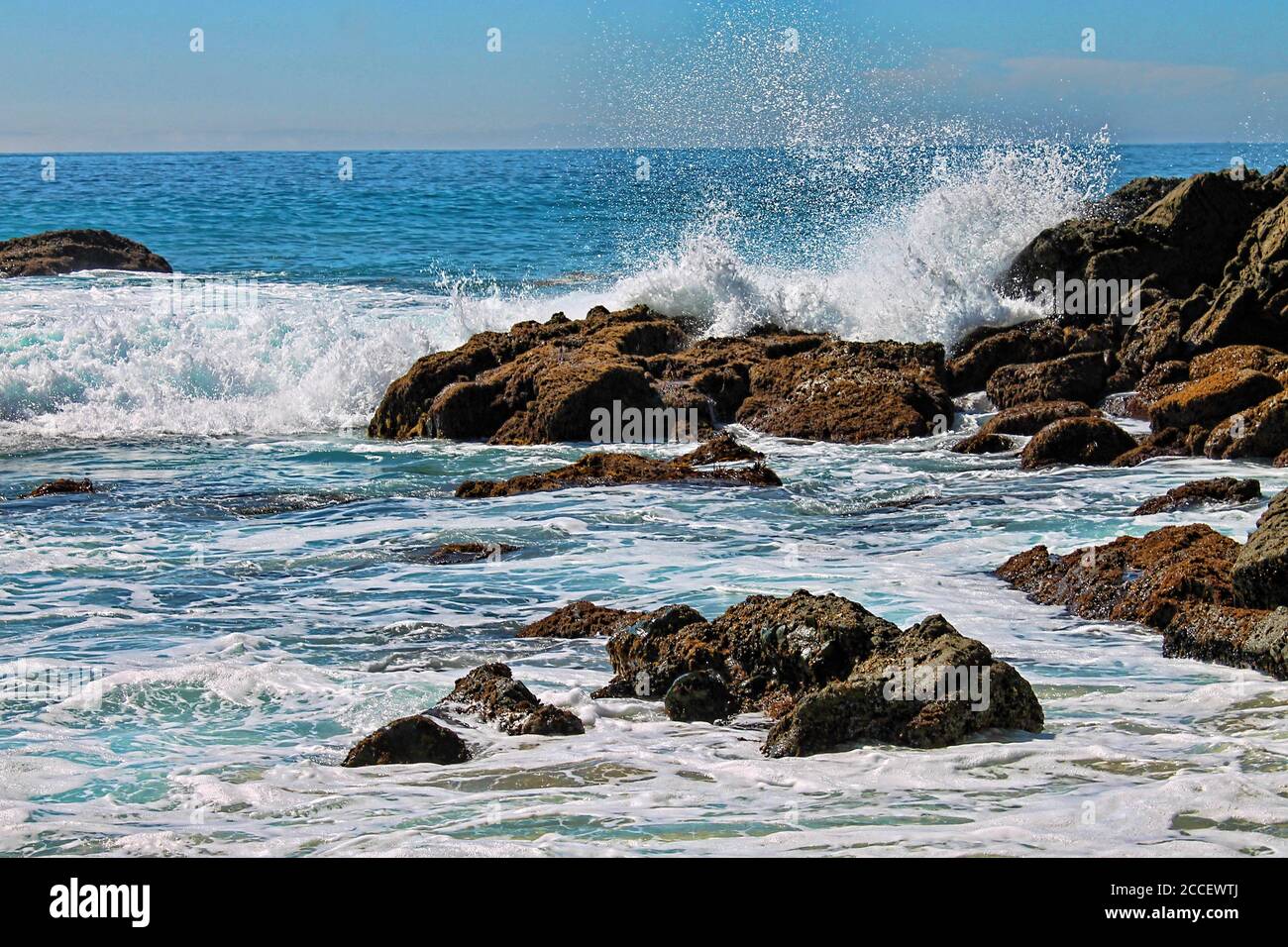 Ocean waves break and splash over sea rocks in a beach cove Stock Photo ...