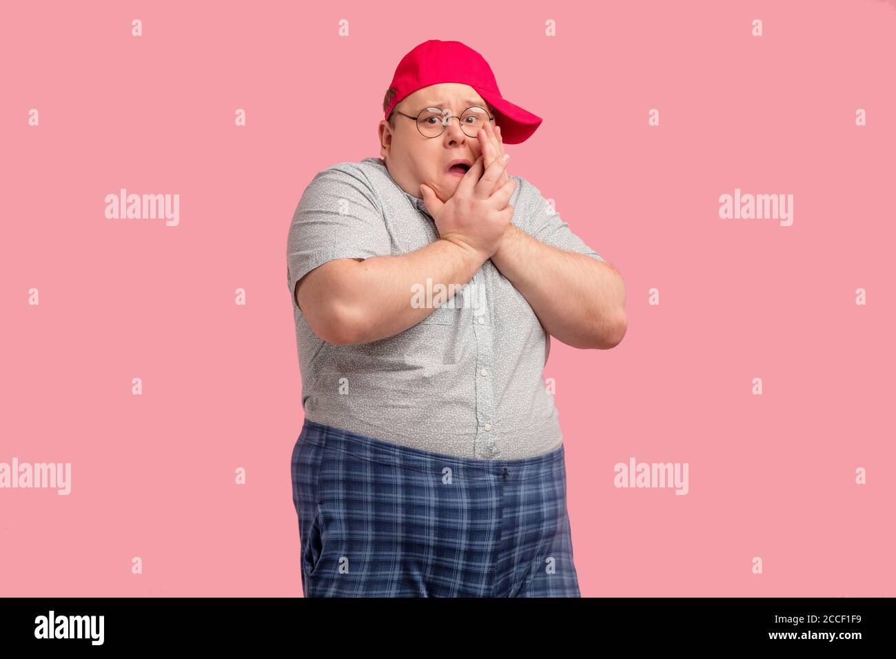 Portrait of surprised, shocked tubby man in red baseball cap looking at ...
