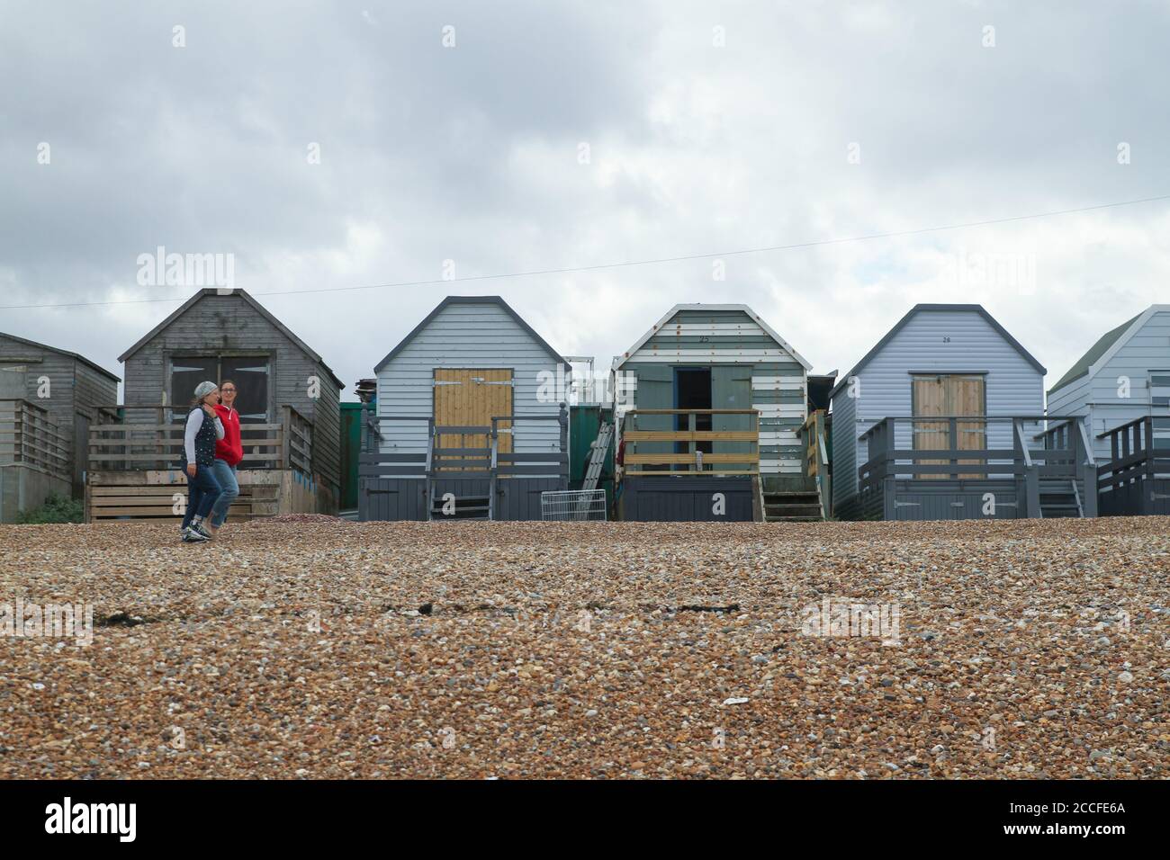 UK. 21st Aug, 2020. Two women walk by beach huts at the pebble beach in ...