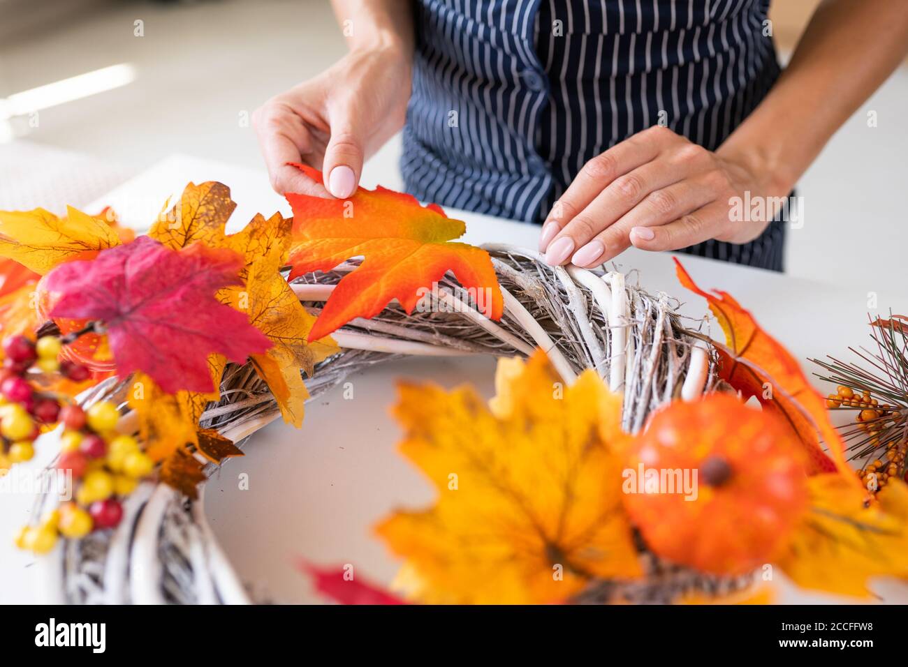 Florist at work: woman makes an autumn wreath at the door from yellow ...