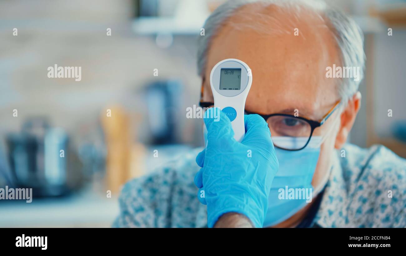 Medical assistance checking senior man body temperature using infrared ...