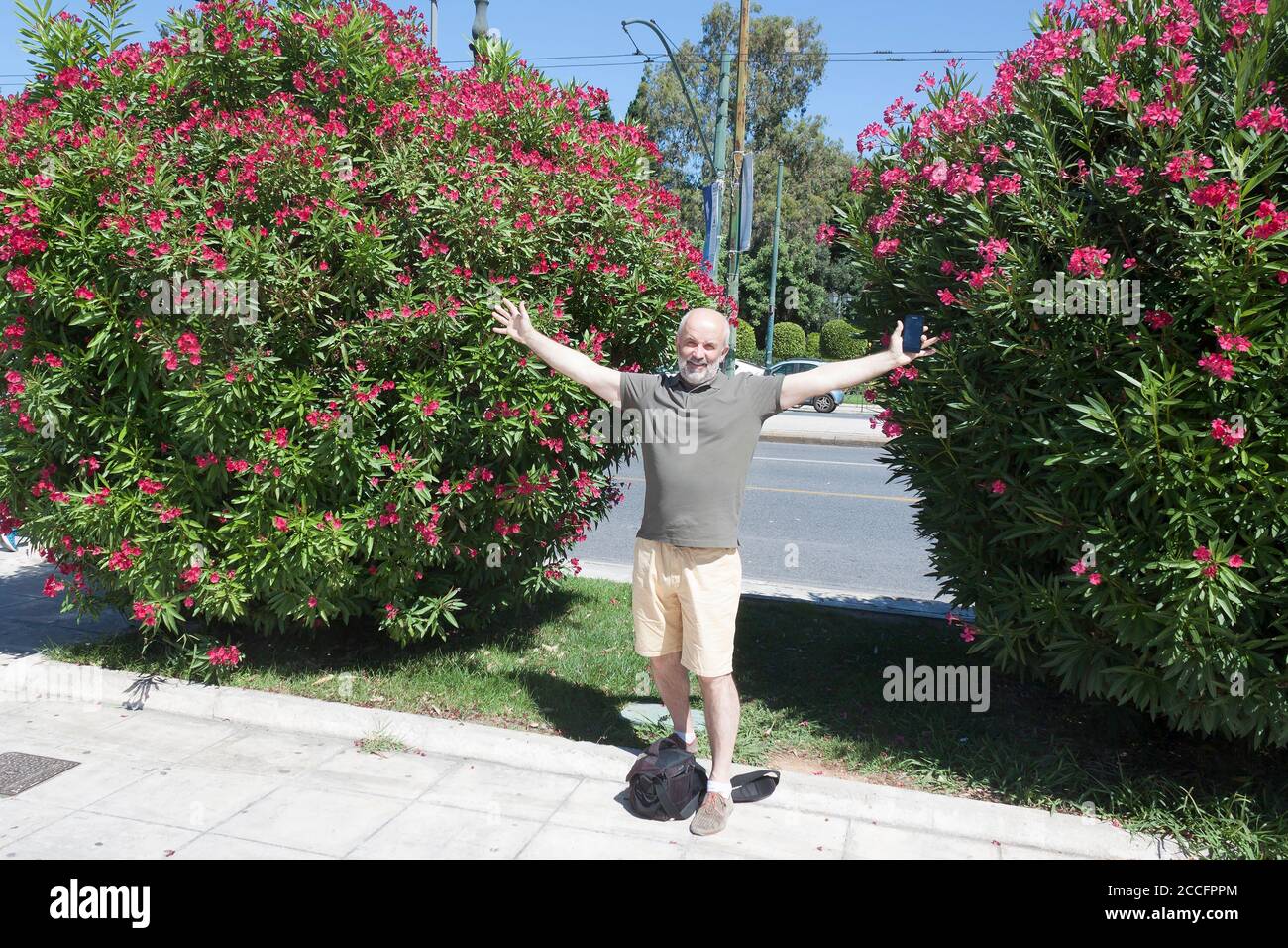 A man of mature age stands waving his arms between two large shrubs ...