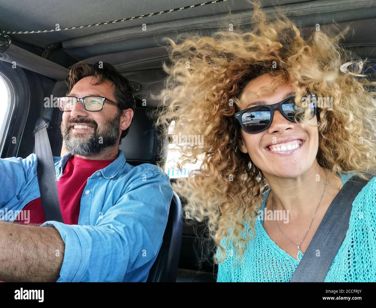 Cheerful couple drive and enjoy the trip inside a car with wind in the ...