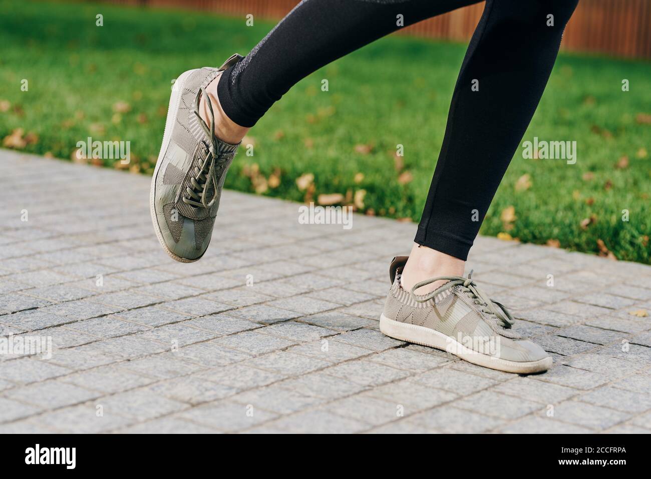 Legs in sneakers and black leggings running long distances in a park in ...