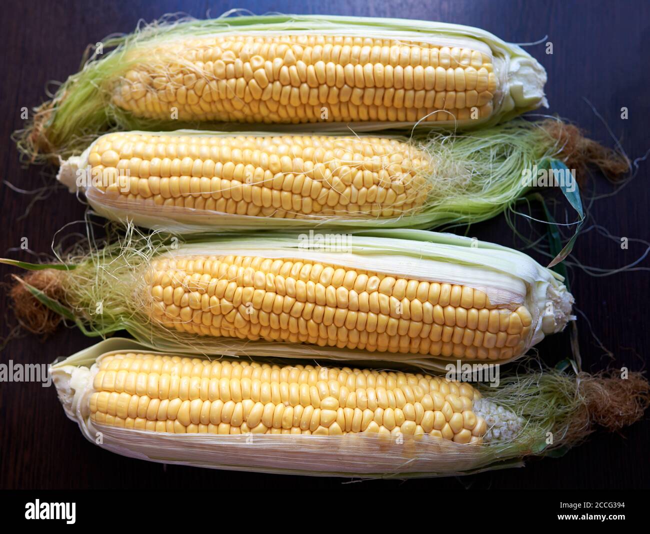 Four golden ears of corn with leaves. Low key. Top view Stock Photo - Alamy