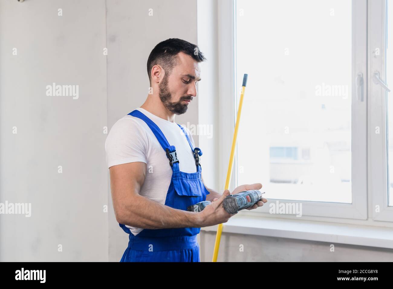A worker in a blue overalls holds a tape measure in his hand Stock ...