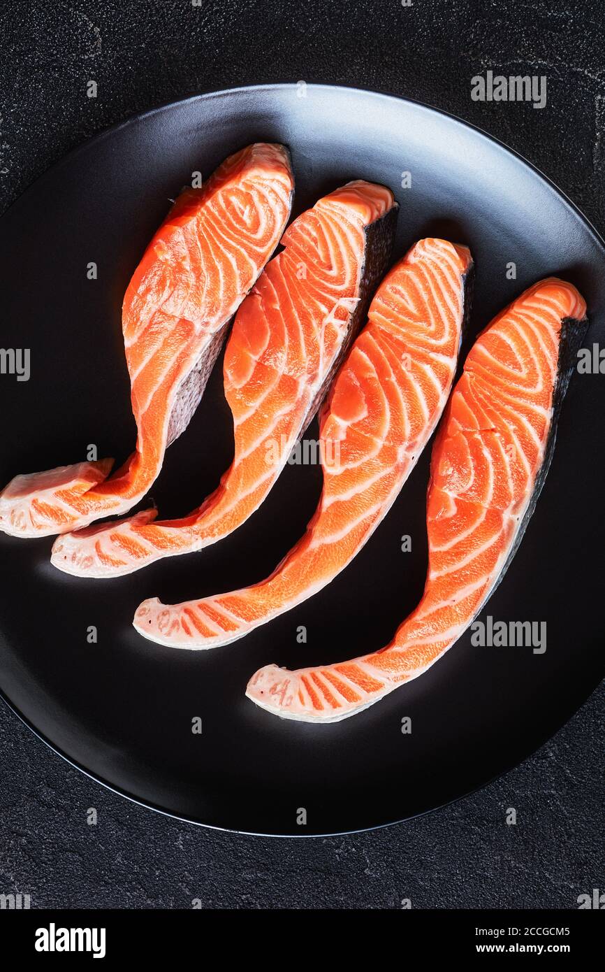 raw salmon fillets on a black plate on a concrete table, vertical view ...