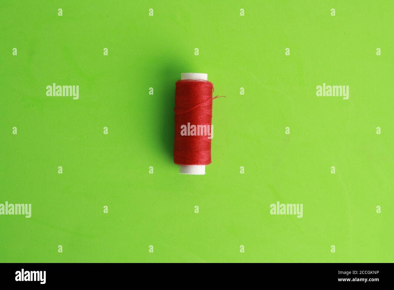 Top view of a red sewing thread on a green background Stock Photo - Alamy
