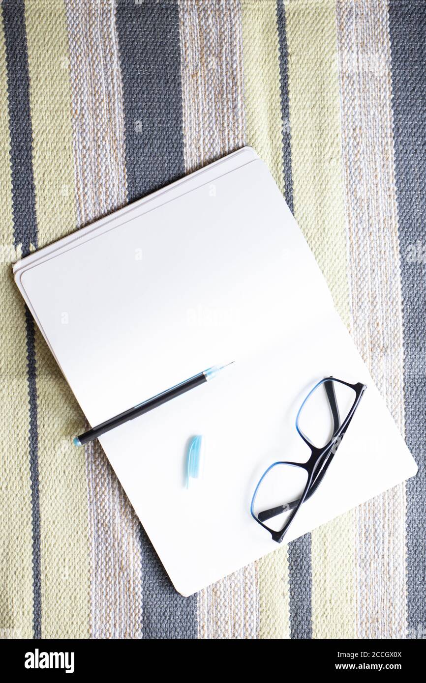 Vertical top view of an opened notebook with pen and eyeglasses on it ...