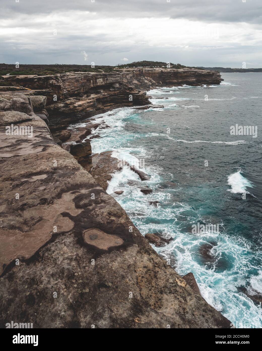 Beautiful vertical shot of a large cliff next to blue water on a gloomy ...