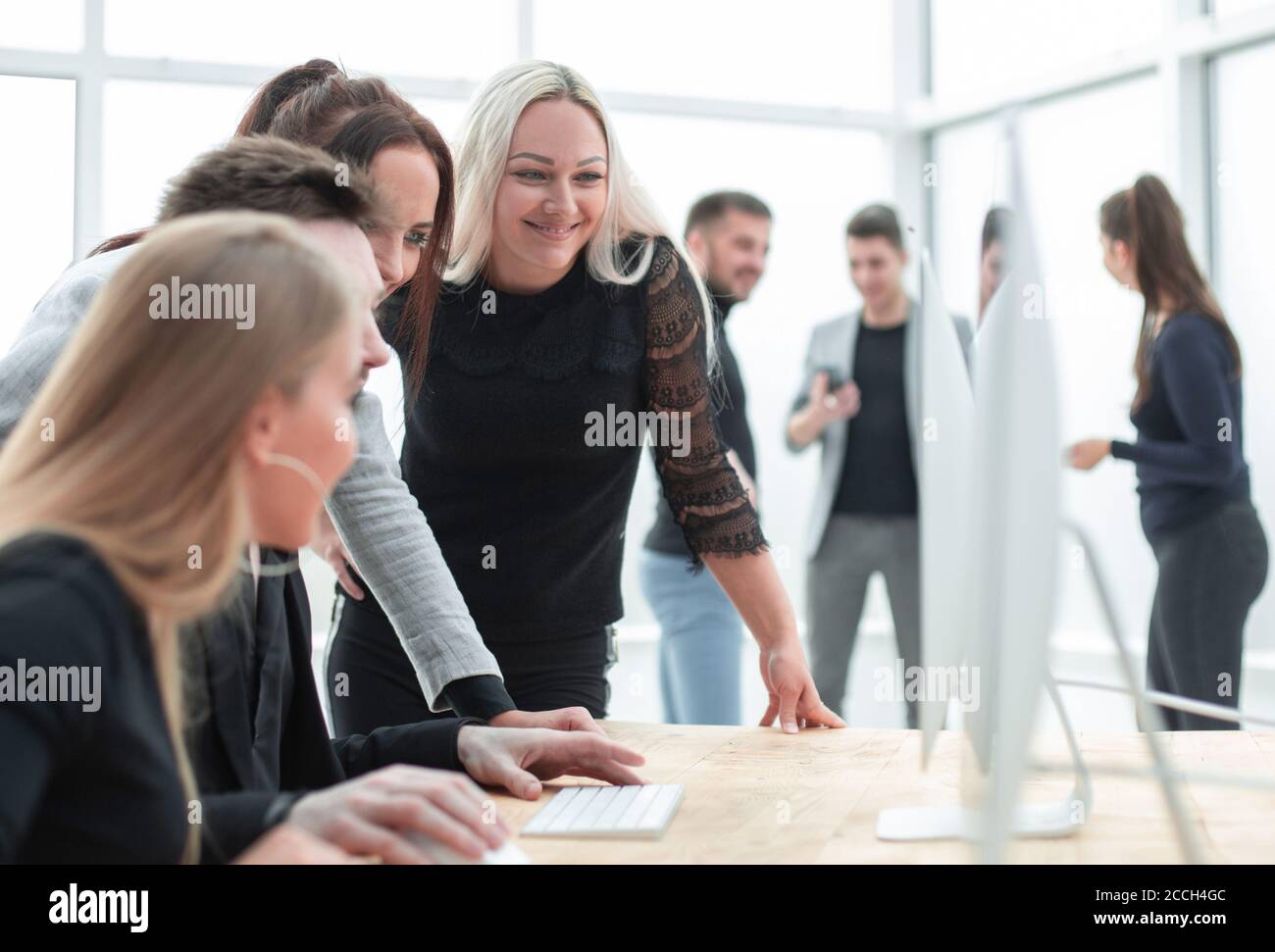 group of young employees looking at the screens of office computers ...