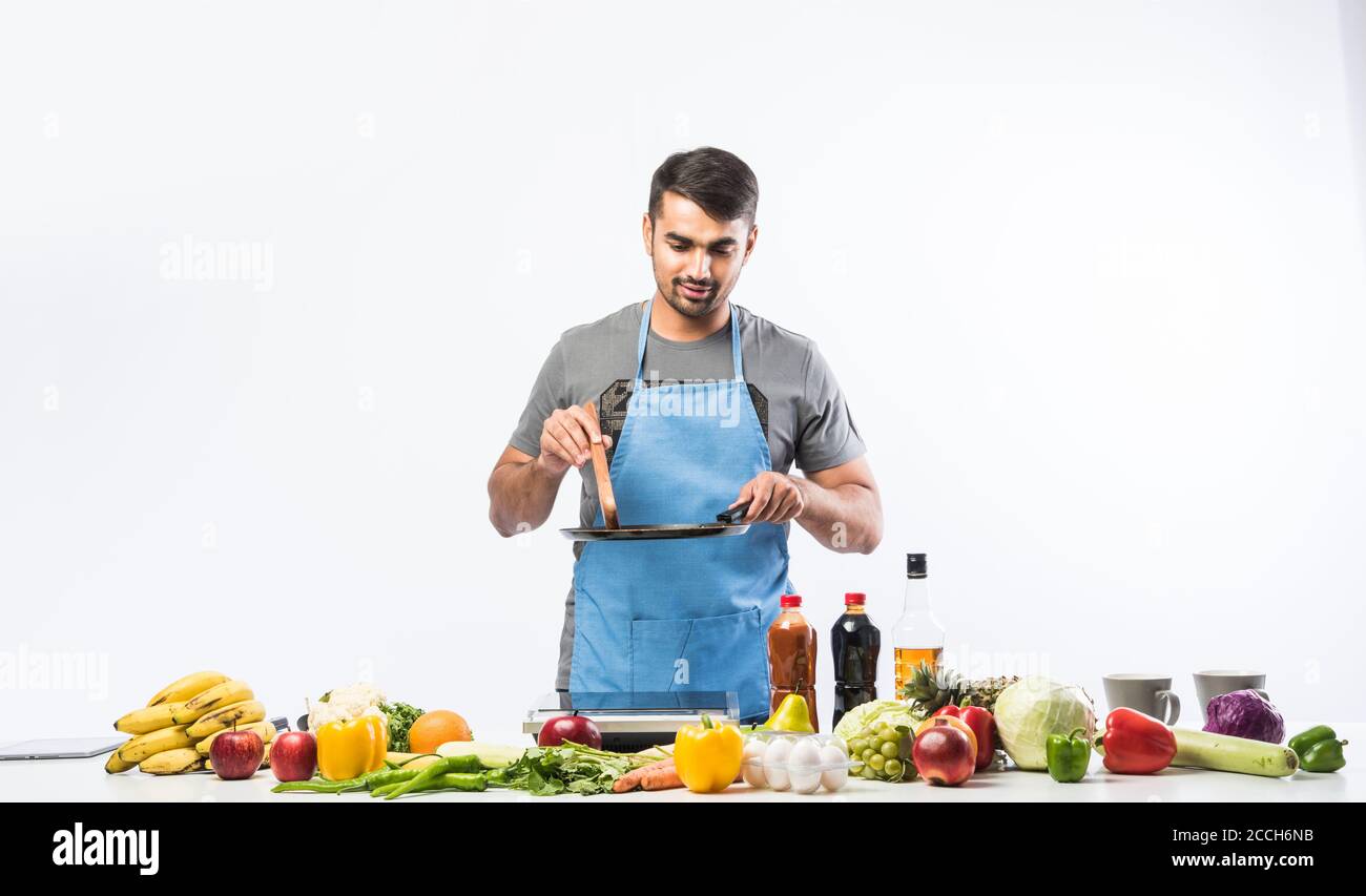 Handsome cheerful smiling indian man preparing meal in the kitchen ...
